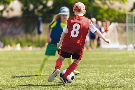 두 명의 남학생이 축구 경기를 합니다 스포티한 모자를 쓴 두 아이가 잔디밭에서 축구공을 차고 있다 여름 캠프에서 축구 훈련 수업 중에 축구 경기를 하는 아이들 10 11세에