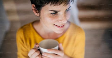 집에서 실내에 커피를 들고 서 있는 젊은 여성의 전면 모습 유리를 통해 촬영했습니다 사진 Unsplash의 컵 이미지