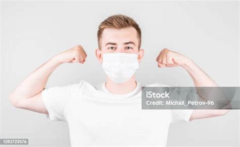 팔을 들어 올려 서 있는 의료용 보호 마스크를 착용한 잘생긴 미국 남자의 초상화는 강한 이두근을 보여줍니다 격리된 배경입니다