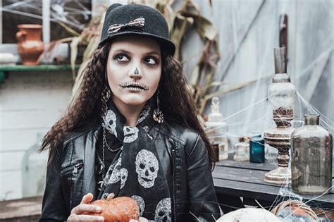 할로윈을 축하하는 아름다운 무서운 어린 소녀 무서운 블랙 화이트 하프 페이스 메이크업 마녀 의상 세련된 이미지 공포 거리의 헛간에서 어린이 파티에서 재미 모자 재킷 호박