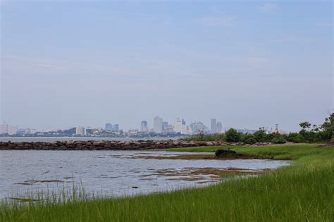 푸른 습지 잔디 잔잔한 바다 바위가 많은 해안선 부드럽고 푸른 하늘 아래 멀리 떨어진 도시 스카이라인이 있는 평화로운 해안 풍경이 도시와 자연 경관이 조화를 이룹니다 0명에