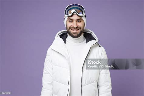 따뜻한 흰색 패딩 윈드 브레이커 재킷 스키 고글 마스크에 미소 스키어 남자는 보라색 배경에 고립 된 산에서 극단적 인 주말 겨울 시즌을 보낼 것입니다 사람들 라이프 스타일