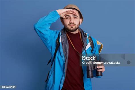 관심있는 활동적인 탐험가가 손으로 이마를 만지고 먼 것을 바라보고 한 손에 쌍안경을 들고 캠핑을 가고 잠자는 패드와 배낭을