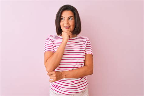 줄무늬 티셔츠를 입은 젊은 아름다운 여성은 턱에 손을 얹고 질문 펜시브 표정을 생각하고 고립 된 분홍색 배경 위에 서 있습니다 미소와 사려 깊은 얼굴 의심 개념 질문하기에