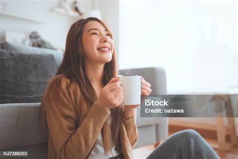 집에서 소파 옆 깔개에 앉아 커피 한 잔을 즐기는 즐거운 젊은 아시아 여성 가을에 대한 스톡 사진 및 기타 이미지 가을