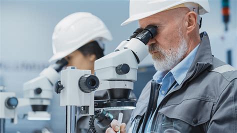중년의 산업 과학 엔지니어는 전자 공장 시설의 책상에서 현미경을 사용하여 소규모 제조 생산 부품 및 세부 사항을 작업합니다 2명에 대한 스톡 사진 및 기타 이미지 Istock