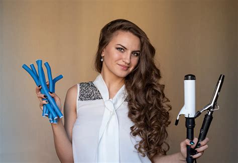 아름다운 젊은 Hairstulist 갈색 머리 와 갈색 머리 들고 푸른 롤러와 철 경기자 그녀의 손에 어느 하나는 곱슬 머리 스타일을 만들기위한 더 나은 선택을하려고 머리