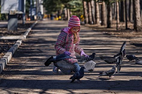 빨간 재킷 모자 및 안경에 있는 소녀 아이는 씨앗으로 공원에서 비둘기를 공급 합니다 소녀는 화창한 봄 날에 공원 골목을 따라 산책 합니다 감정에 대한 스톡 사진 및 기타