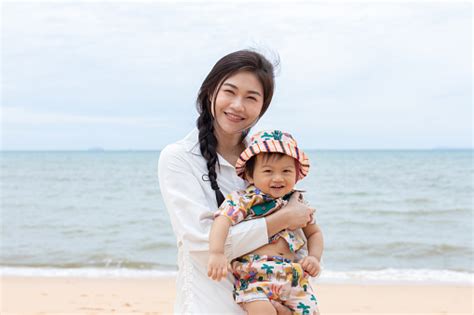 행복한 아시아 엄마와 아기는 아름다운 바다로 카메라를 보며 미소 지었다 가족 어머니와 아기가 함께 시간을 보내는 휴가는 해변에서 즐깁니다 좋은 순간 야외 활동 긍정적 인
