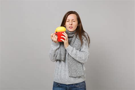 회색 스웨터에 젊은 여자 눈 감고 스카프 레몬 차 회색 배경에 고립의 빨간 컵 개최 건강 패션 라이프 스타일 사람들이 진심으