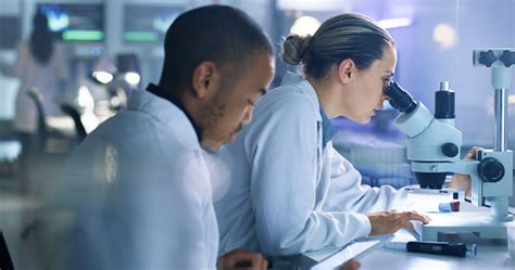 현대 실험실에서 실험실 코트를 입은 심각한 남성과 여성 과학 전문가는 현미경을 사용하여 페트리 접시를 분석합니다 실험을 수행하는 연구 분야의 과학자 팀 의료 연구에 대한