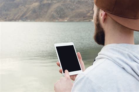 야외에서 갈색 모자에 다발의 클로즈업 그의 손에 흰색 태블릿 Pc를 보유 하고있다 턱수염이 난된 남자는 태블릿에 보인다 Ots는 어깨 뒤에서 보기 스왑 자신의 손가락으로