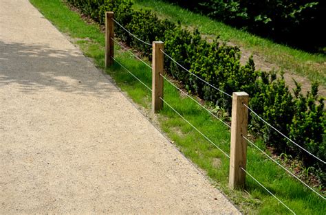 세 개의 강철 밧줄과 나무 기둥이있는 낮은 울타리가 자갈 길과 잔디밭을 분리하고 도시 공원에 있는 박스 우드가있는 화단은 개를 입력하지 않도록 보호합니다 0명에 대한 스톡