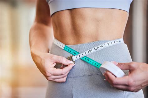 줄자 배 그리고 체중 감량을 위한 체육관의 여성 다이어트 또는 흐릿한 배경에서 운동 피트니스 측정 및 소녀는 훈련 운동 또는 건강한 생활 습관 결과에서 평평한 배꼽에 모형에