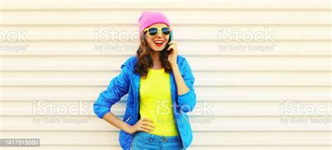 화려한 분홍색 모자를 쓰고 스마트폰을 신고 전화하는 행복한 미소 짓는 젊은 여성의 초상화 흰색 배경에 파란색 재킷 20 29세에 대한 스톡 사진 및 기타 이미지 Istock