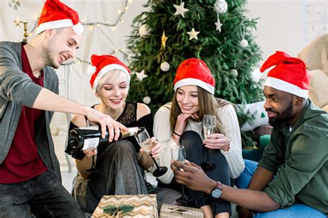 젊은 아프리카 남자와 백인 남자와 여자 20 받는 사람 30 세 산타 모자 와 함께 크리스마스 또는 크리스마스와 새해 축 하 파티에 대 한 샴페인을 마시는 안경을 Clink