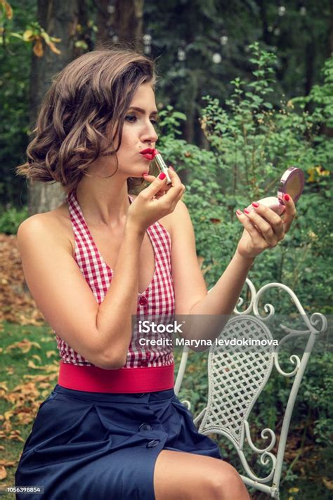 핀업 소형 거울을 보고과 립스틱 소녀 모델은 빨간색과 흰색 체크 무늬 탑 넓은 붉은 벨트 파란 치마 입고 배경에 녹색 공원입니다 개성 개념에 대한 스톡 사진 및 기타 이미지