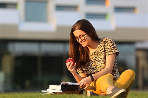 배낭과 책 잔디밭에 앉아서 먹는 사과와 안경에 젊은 여성 학생 젊은 여성 야외 점심을 있다 건축물에 대한 스톡 사진 및 기타 이미지 Istock