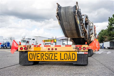 강력한 대형 장비 클래식 세미 트럭 스텝 다운 세미 트레일러에서 대형 장비를 운반 트럭 정류장 주차장에 나머지를 위해 서있는 뒷면에 대형 적재 표지판 트럭에 대한 스톡 사진