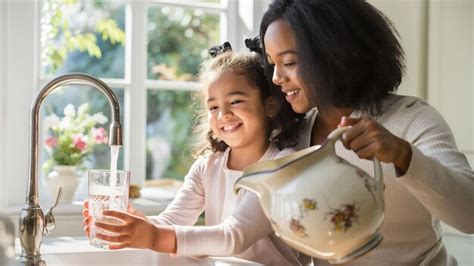 Smiling Girl Holding Glass While Her Mother Pouring Water Premium Ai