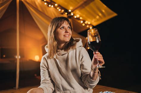 웃는 여성 프리랜서가 와인을 마시고 가을 저녁에 아늑한 글램핑 텐트에 앉아 책을 읽었습니다 야외 휴가 및 휴가를위한 고급 캠핑 텐트 라이프스타일 개념 관광에 대한 스톡 사진