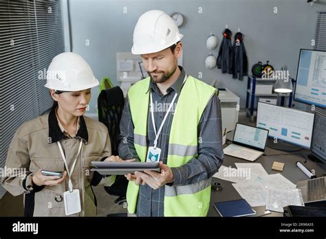 Waist Up Portrait Of Two Engineers Wearing Hardhats Indoors And