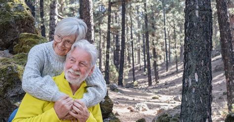 손을 잡고 숲에 앉아 있는 아름다운 행복한 노부부 백인 여자는 웃고 있는 남편을 껴안고 있다 화창한 날에 휴가의 자유와 자연 하이킹을 즐기는 노인 회색 머리 사람들 사진