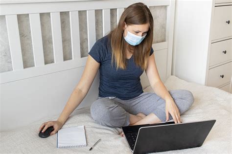 자체 격리에 대한 원격 작업 의료 얼굴 마스크에 귀여운 젊은 십대 소녀 또는 여자는 집에서 편안하고 메모장에 쓰기에서 작동합니다 노트북을 사용하는 여학생 검역소에서의 원격