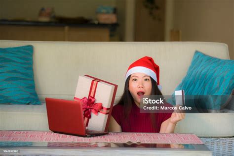 젊고 아름 다운 행복 한 아시아 한국 여자 산타 모자 신용 카드와 크리스마스 선물 상자 선물에 대 한 인터넷 온라인 쇼핑 웃 고 사는 가정에서 랩톱 컴퓨터를 사용 하 여