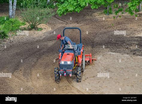A Farmer On A Mini Tractor Loosens The Soil For The Lawn Land