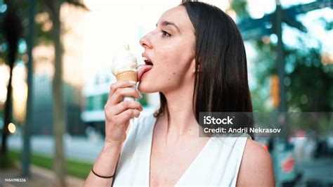 주근깨와 어두운 느슨한 머리카락을 가진 클로즈업 아름다운 여자는 화이트 탑 테스트 아이스크림을 착용합니다 귀여운 소녀는 현대 도시 배경에 아이스크림을 즐긴다 도시에 대한