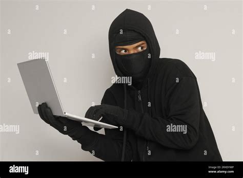 Portrait Of Mysterious Man Wearing Black Hoodie And Mask Doing Hacking Activity On Laptop