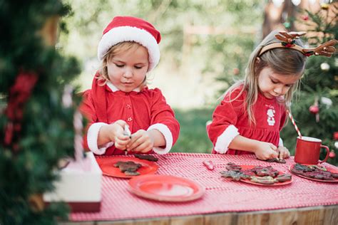 산타 모자를 쓴 두 소녀가 진저 브레드 쿠키를 색칠하고 밖에서 핫 초콜릿을 마시며 재미를 느낍니다 2명에 대한 스톡 사진 및 기타 이미지 Istock