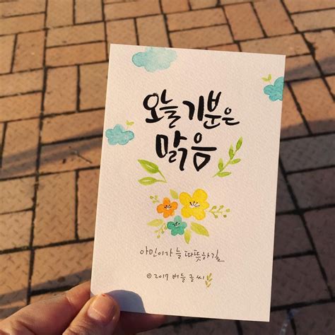 A Person Holding Up A Card With The Words Hello In Korean On It And Flowers