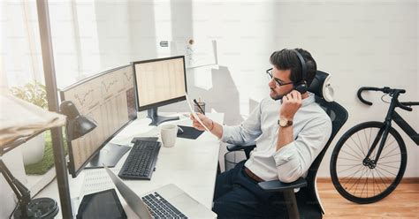 사업에 대해 이야기합니다 헤드셋을 쓴 젊은 수염 난 상인이 재무 보고서를 들고 사무실의 모니터 화면 앞에 앉아 고객과 이야기하는 측면 모습 사업 개념입니다 무역