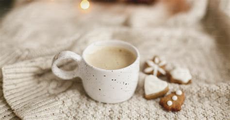 크리스마스 진저 브레드 쿠키와 따뜻한 조명이있는 아늑한 니트 스웨터를 배경으로 세련된 컵에 따뜻한 커피 대기 겨울 휘게