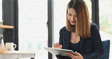 컴퓨터 태블릿과 스타일러스 펜을 손에 들고 사무실 유리 벽을 배경으로 현대적인 작업 테이블에 앉아 있는 임원 여성 사진 Unsplash의 태국 이미지