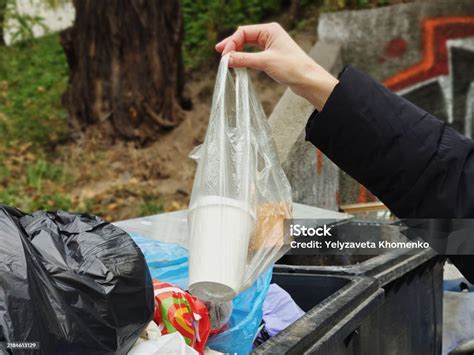 사람의 손이 투명한 쓰레기 봉투를 길거리의 커다란 검은색 플라스틱 쓰레기통에 던지고 있다 본인은 쓰레기를 꺼내 쓰레기 봉투를
