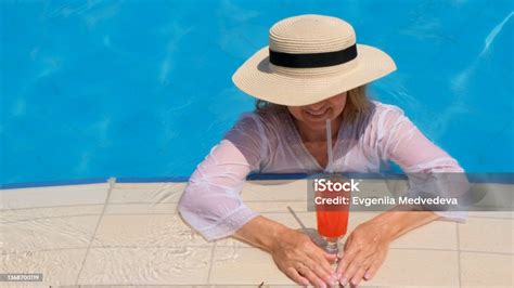 밀짚 모자를 쓴 금발 의 여인이 화창한 여름날 수영장 근처에서 휴식을 취하고 오렌지 칵테일을 마십니다 여름 무드 컨셉 휴가 모든