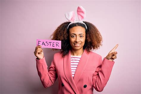 아프리카계 미국인 여성 Afro 머리 입고 토끼 귀 들고 종이 와 메시지 매우 행복 가리키는 손과 손가락 으로 측면 가리키기에