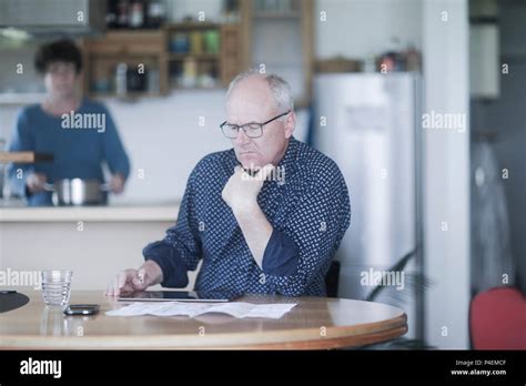 Man Sitting At Table Working While His Wife Prepares Food Stock Photo Alamy