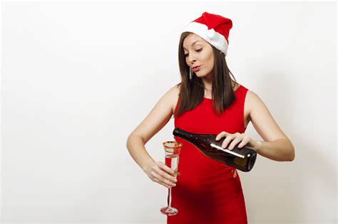 아름 다운 백인 젊은 행복 한 여자 빨간 드레스와 흰색 바탕에 유리에 병에서 크리스마스 모자 붓는 샴페인에 매력적인 미소로 산타 소녀 격리입니다 새 해 2018 휴일