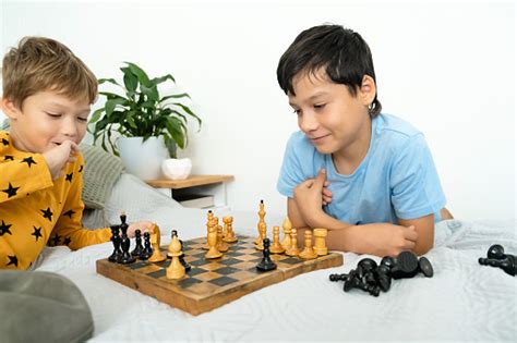 두 명의 백인 소년이 침대에서 집에서 체스를하고 있습니다 형은 어린 아이에게 체스를 가르치고있다 레저 게임 12 13세에 대한