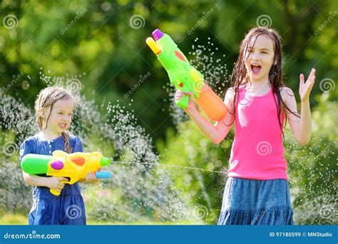 Прелестные маленькие девочки играя с водяными пистолетами на горячий летний день Милые дети имея