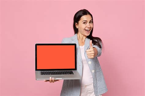 분홍색 파스텔 배경에 고립 된 빈 빈 화면으로 노트북 Pc 컴퓨터를 들고 엄지손가락을 보여주는 줄무늬 재킷의 쾌활 한 여자 사람들은 진심으로 감정 라이프 스타일 개념입니다