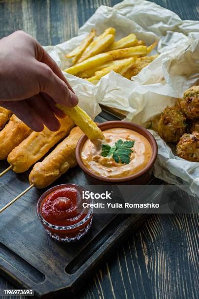 프렌치 프라이 소스를 곁들인 남성 손 튀긴 감자 튀김 개 옥수수와 양배추 크로켓과 소스감자 배경에 신선한 야채와 채소로 장식 된 케첩 패스트 푸드 움직이는 사진 어두운 나무