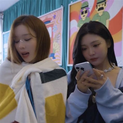 Two Girls Looking At Their Cell Phones In A Room With Posters On The