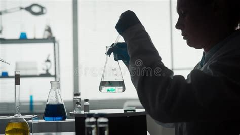 Side View Of A Dark Silhouette Of A Female Scientist Looking Under A Microscope Doing An