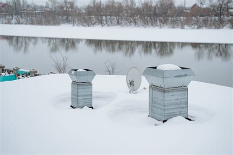 쌀쌀한 겨울날 두 개의 굴뚝이 자연 그대로의 눈으로 아름답게 덮여 있으며 고요한 강 옆에 위치한 지붕 위에 우뚝 서서 얼음으로 뒤덮인 주변 환경을 반사합니다 0명에 대한