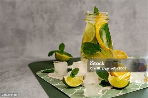 회색 배경에 라임 레몬 민트 얼음 조각이 있는 유리병에 담긴 시트러스 디톡스 차 여름 레모네이드를 만드는 컨셉 감귤류 과일에